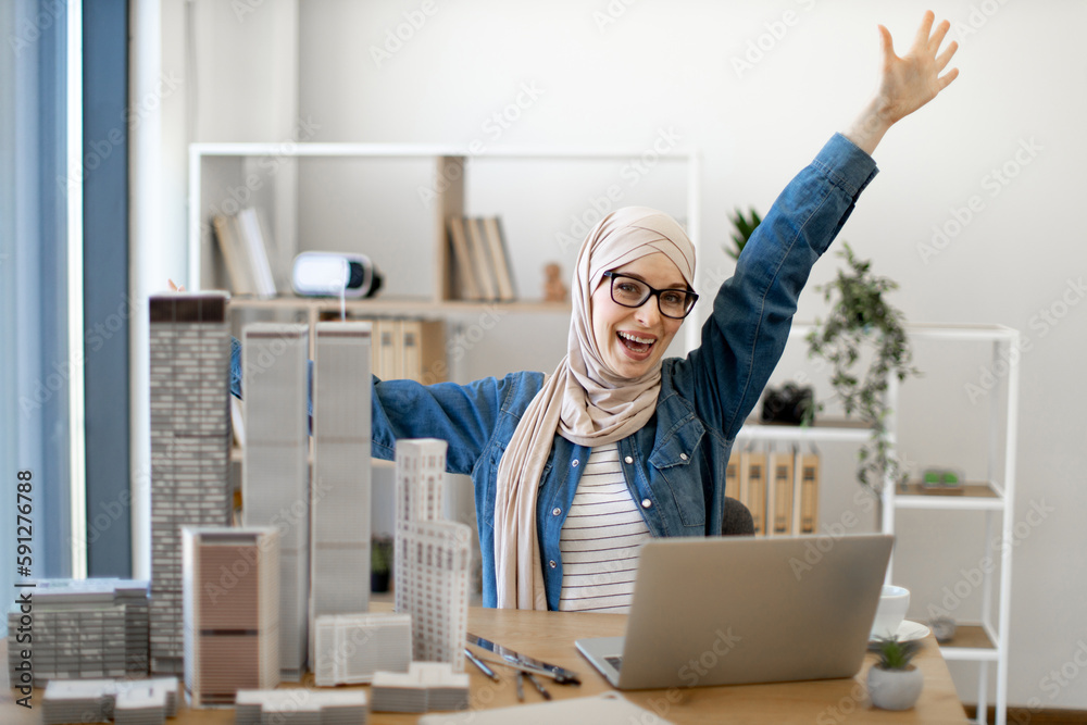 Happy arabian female wearing hijab and spectacles raising arms in ...