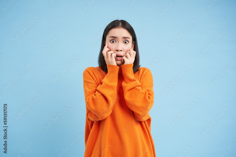 Scared Asian woman shuts her eyes and peeks through hands at smth scary ...