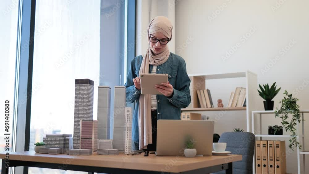 Joyful muslim female in hijab and glasses holding modern tablet while ...
