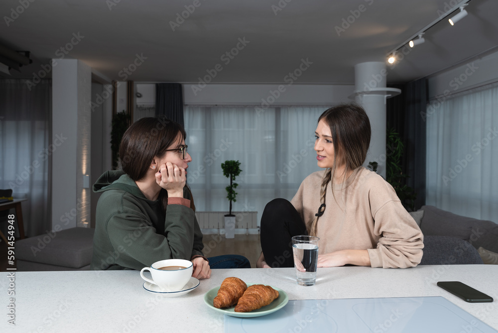 Two millennial girl friends at home talking, drinking coffee ...