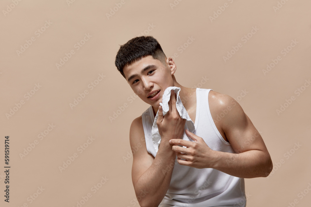 Portrait of young handsome man wiping face after shaving, taking care ...