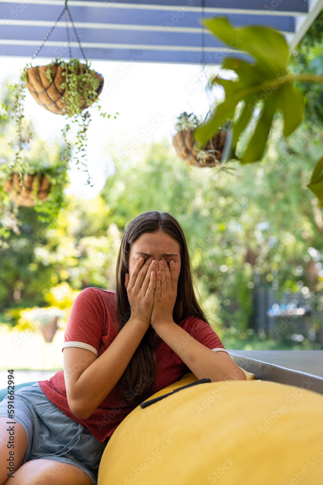 Sad caucasian teenager girl sitting on sofa, covering her face and ...