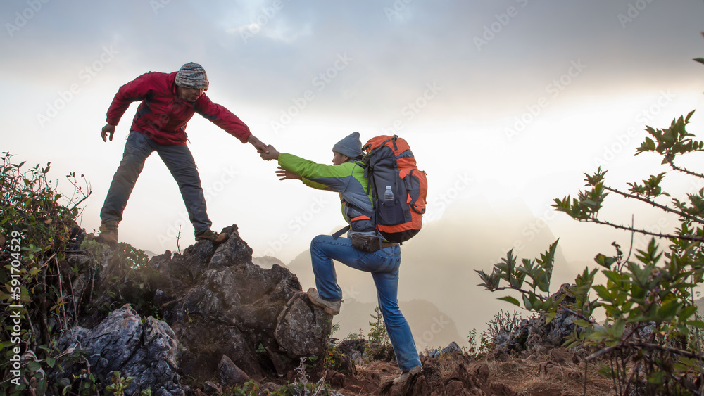 Two Male hikers climbing up mountain cliff and one of them giving ...