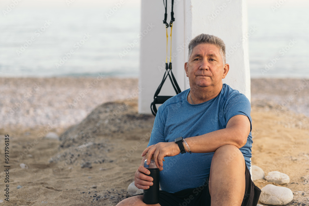 Overweight older white-haired man sitting on the sand of the beach ...