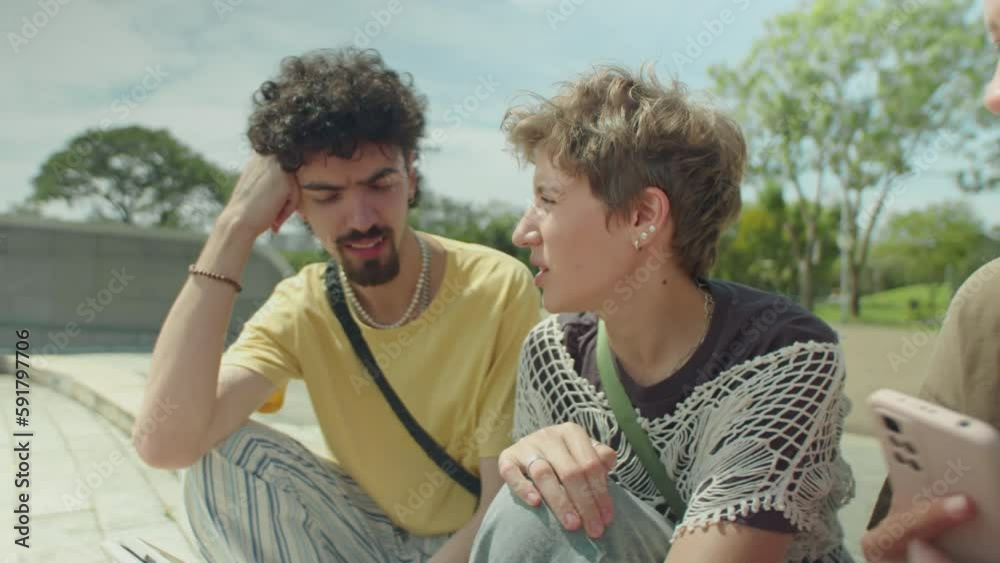 Group of gen Z friends sitting outdoors in city on summer day, using ...