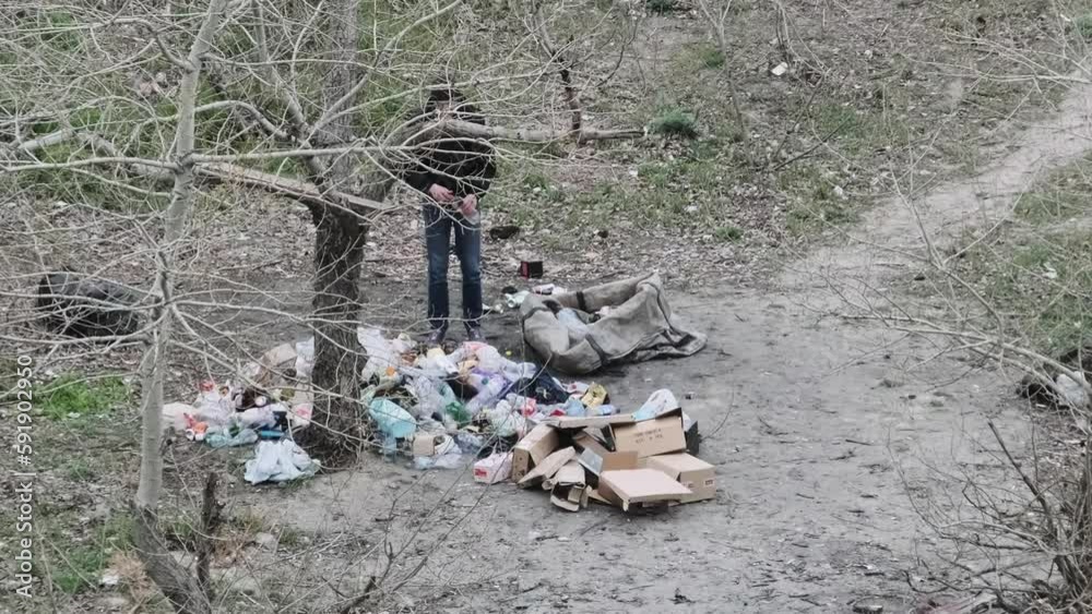 A homeless man rummages through the garbage sorting plastic bottles ...