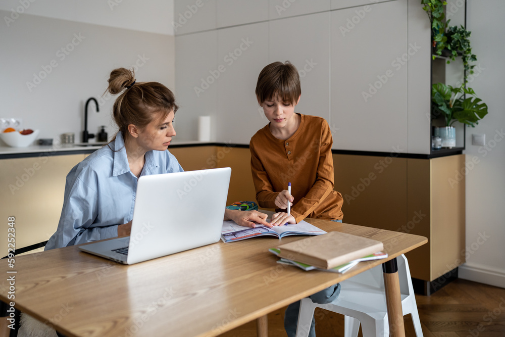 Working mom doing job on laptop and homework with son on kitchen at ...