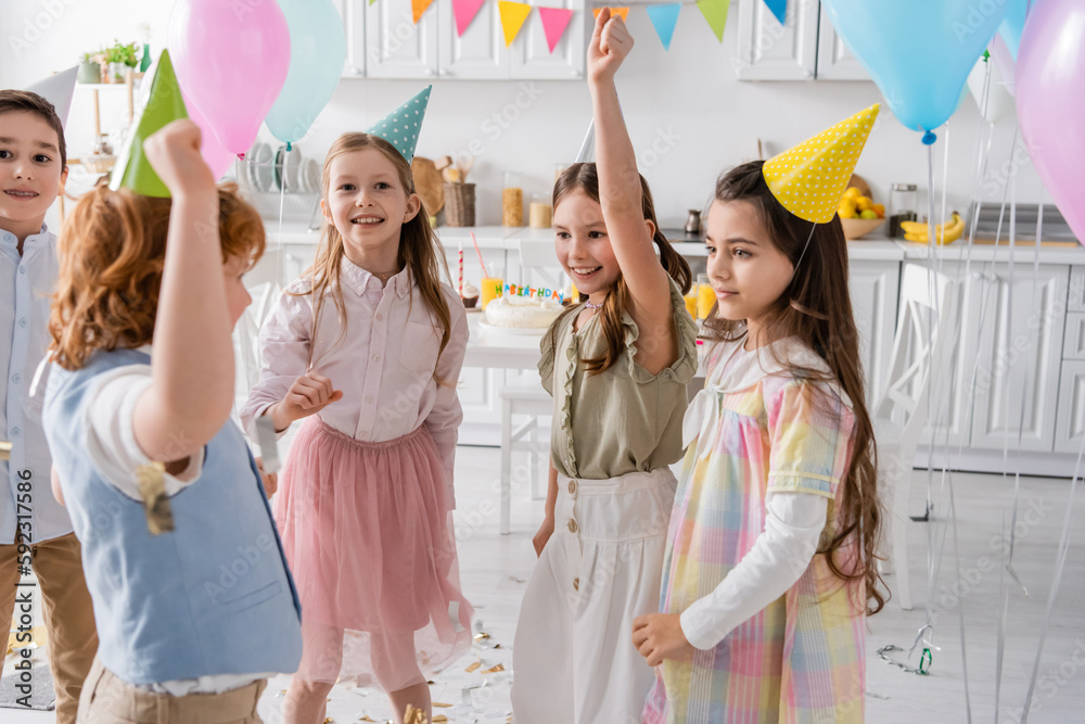 group of happy children in party caps dancing during birthday ...