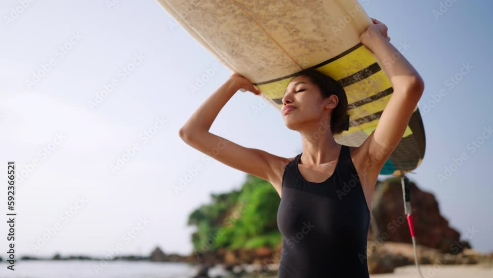 African american woman walking with surfboard on her head on ocean ...