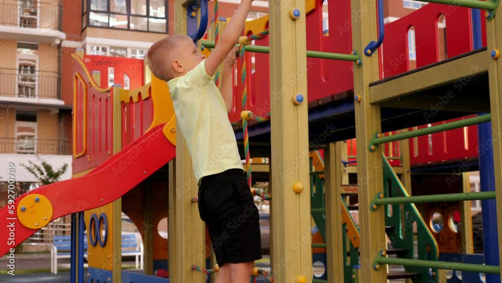 A child climbs a grid in a park on a playground on a hot summer day ...