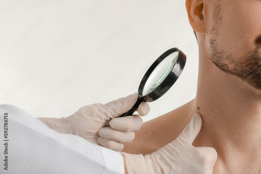 Dermatologist examining mole of young man with magnifier on white ...