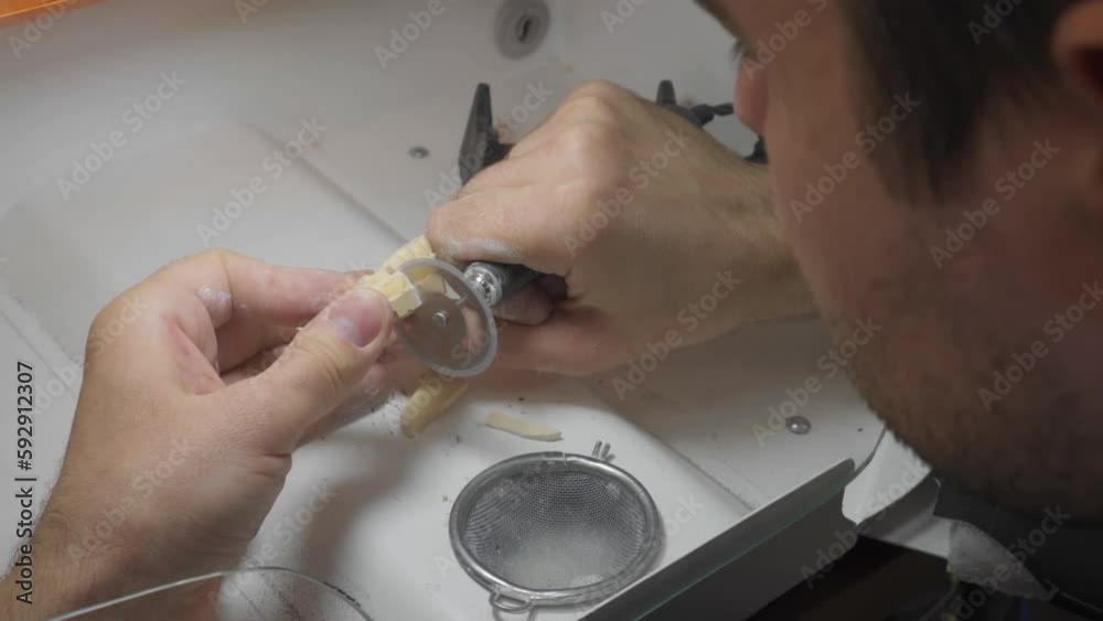 Worker is operating the cutting device to create prosthetic teeth ...