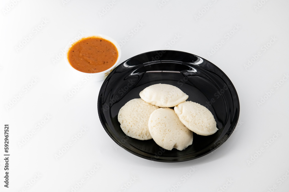 Hot and steaming idly in a black plate and tomato chutney in a isolated ...