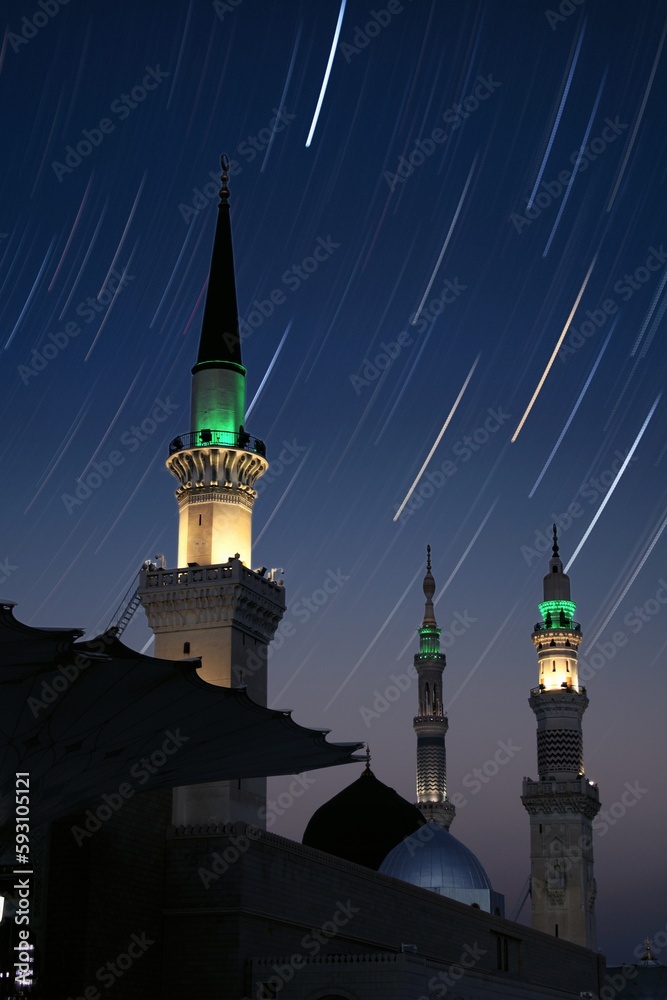 A mosque with green and white lights and a star trails in the sky ...