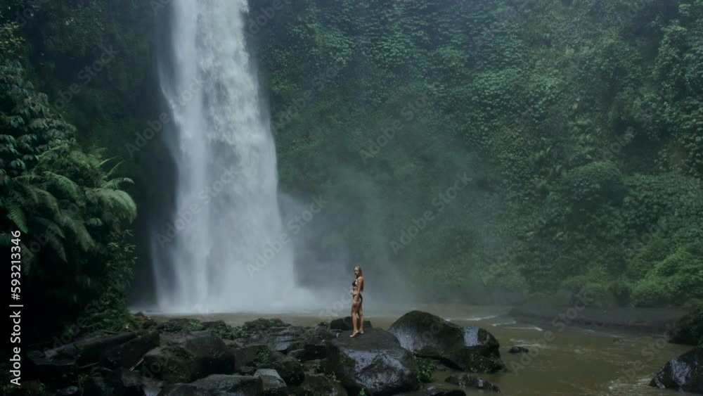 Tropical powerful waterfall in the depth of Bali jungle. Woman tourist ...
