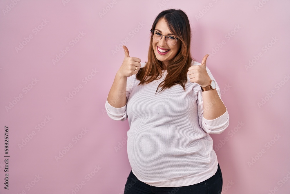 Pregnant woman standing over pink background success sign doing ...