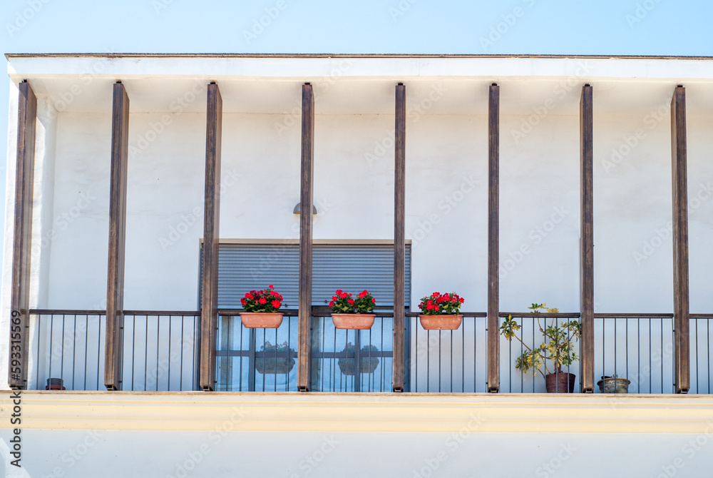 Balcón en edificio blanco, con columnas de madera y tiestos con flores ...