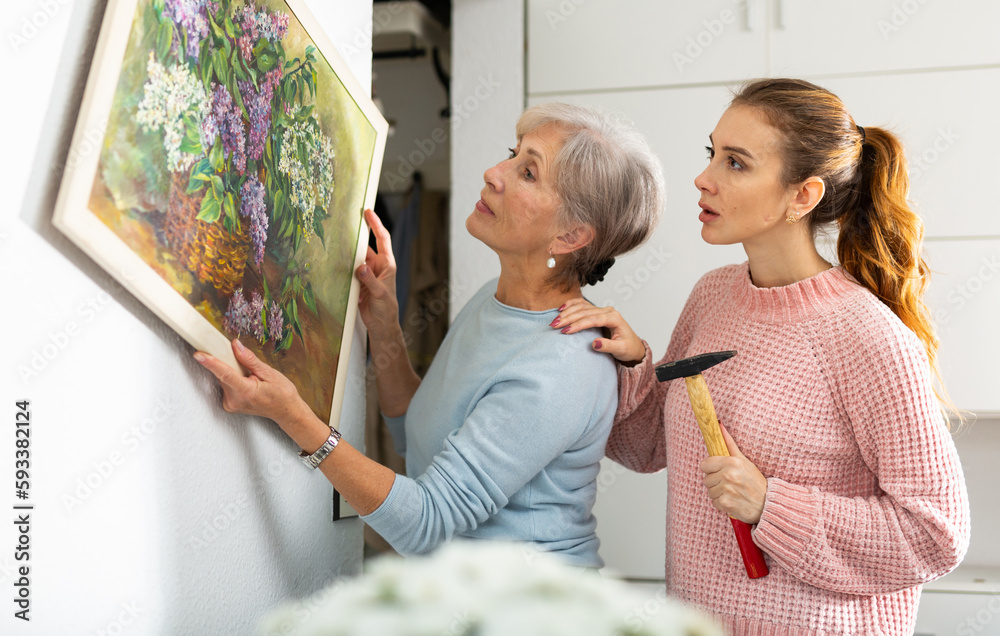 Senior woman trying to put picture on wall. Her granddaughter standing ...