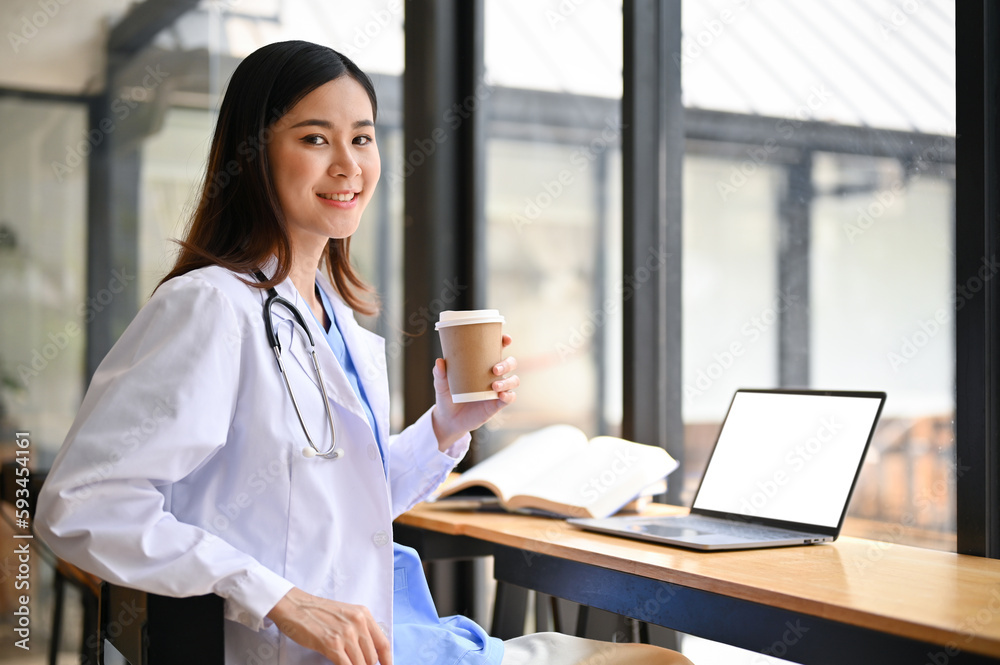 Beautiful Asian female doctor in a uniform has a coffee at a cafe for ...