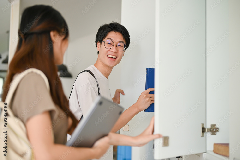 Cheerful Asian male college student talking with his friend at a school ...