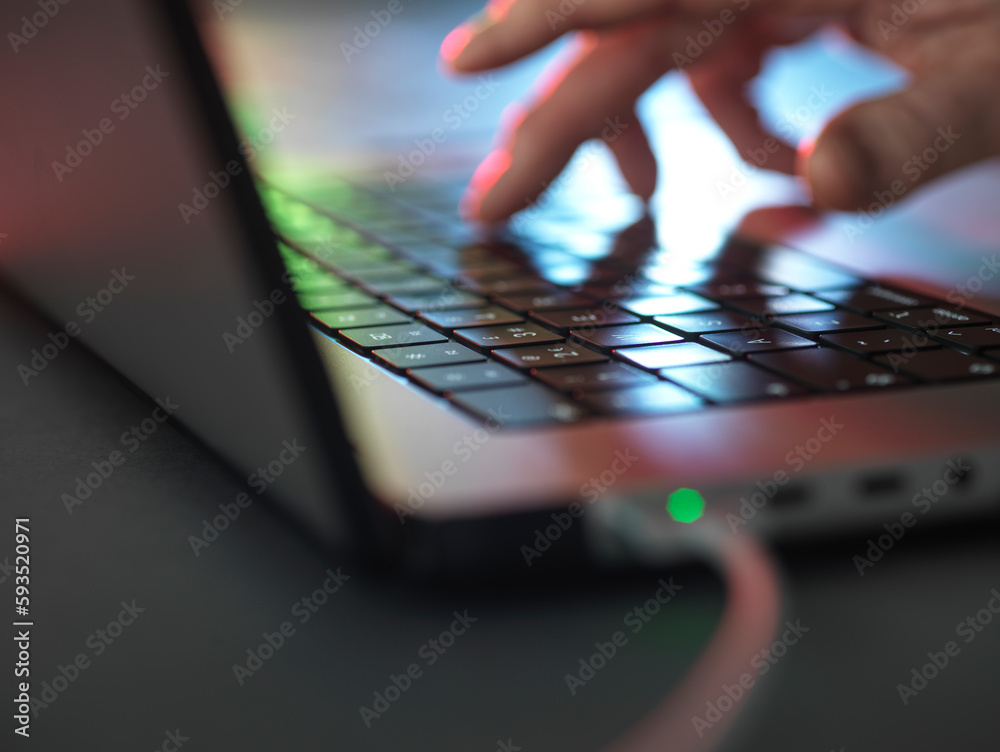 Hands typing on illuminated laptop keyboard in dark at home office ...