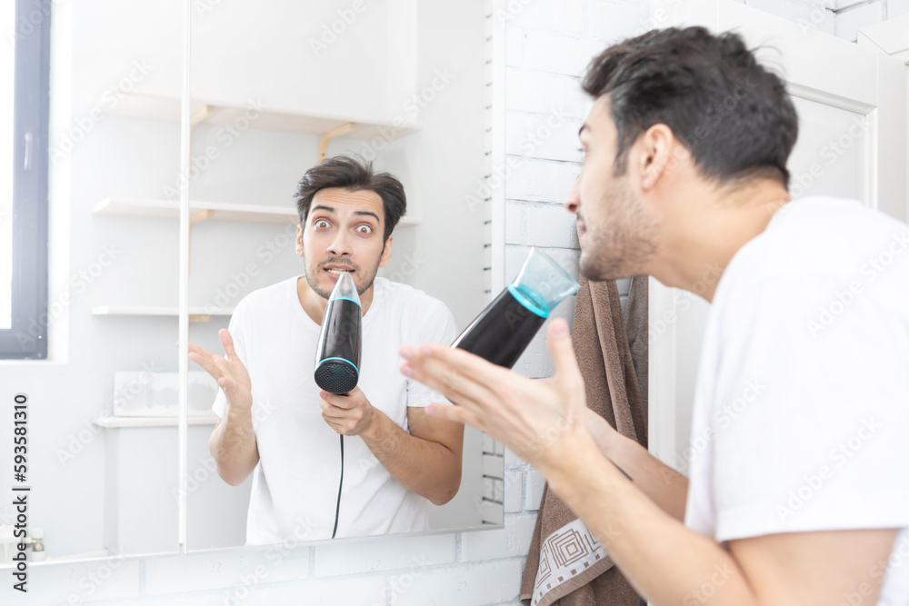 Young handsome man standing in front of the mirror in the bathroom and ...