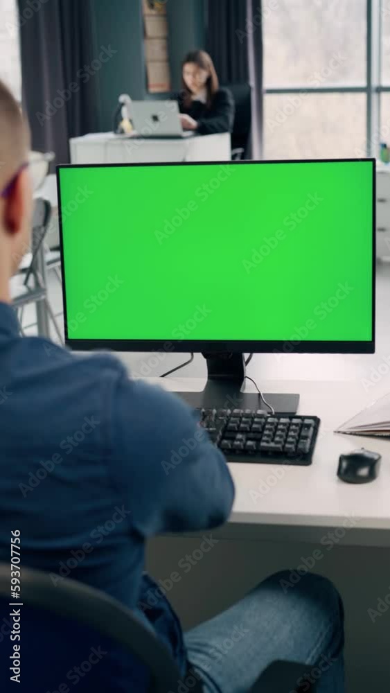 Young Man Working At Computer With Green Mock Up Screen in Office ...