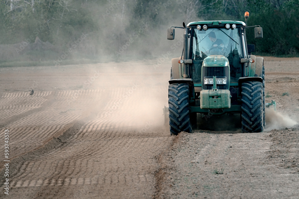 Tractor ploughing a field shrouded in the dust of dry soil from the ...