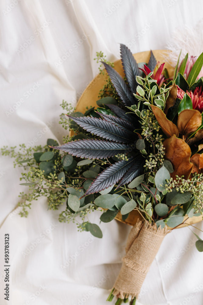 Floral bouquet with purple cannabis leaves on a white linen backdrop ...