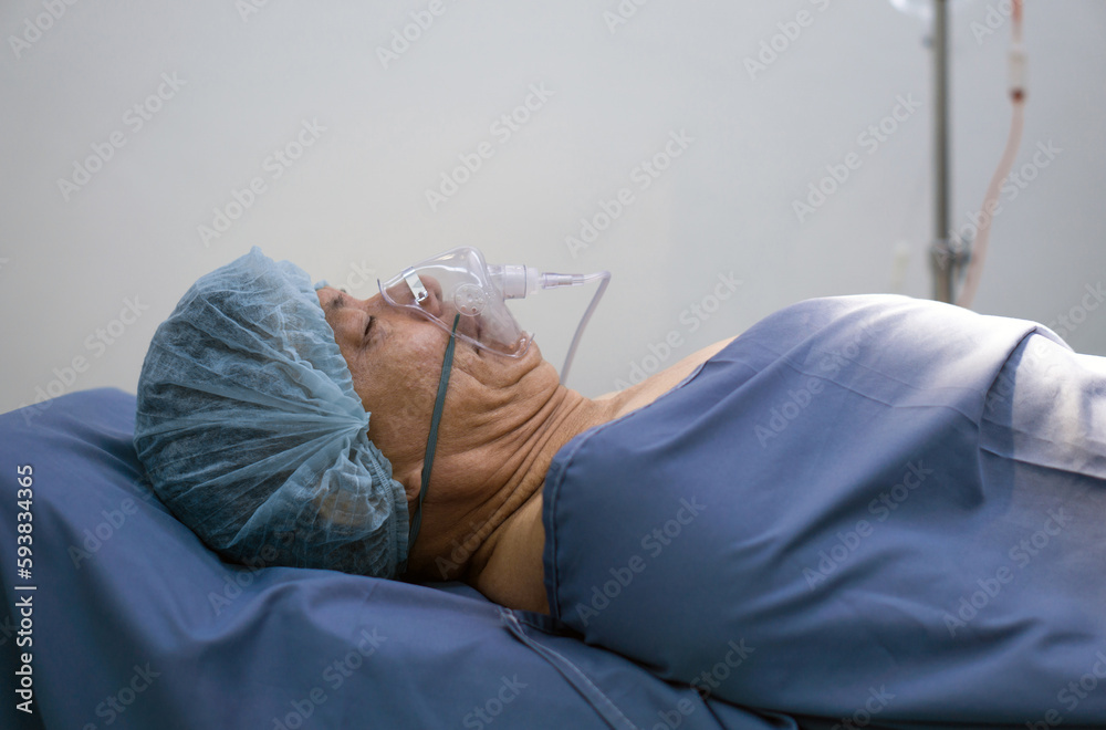 Asian senior patient breathing with respirator, lying on hospital bed ...