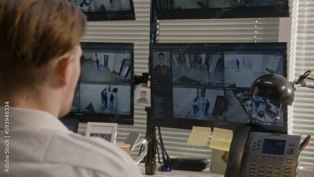 Security officer monitors office CCTV cameras on computers, uses walkie ...