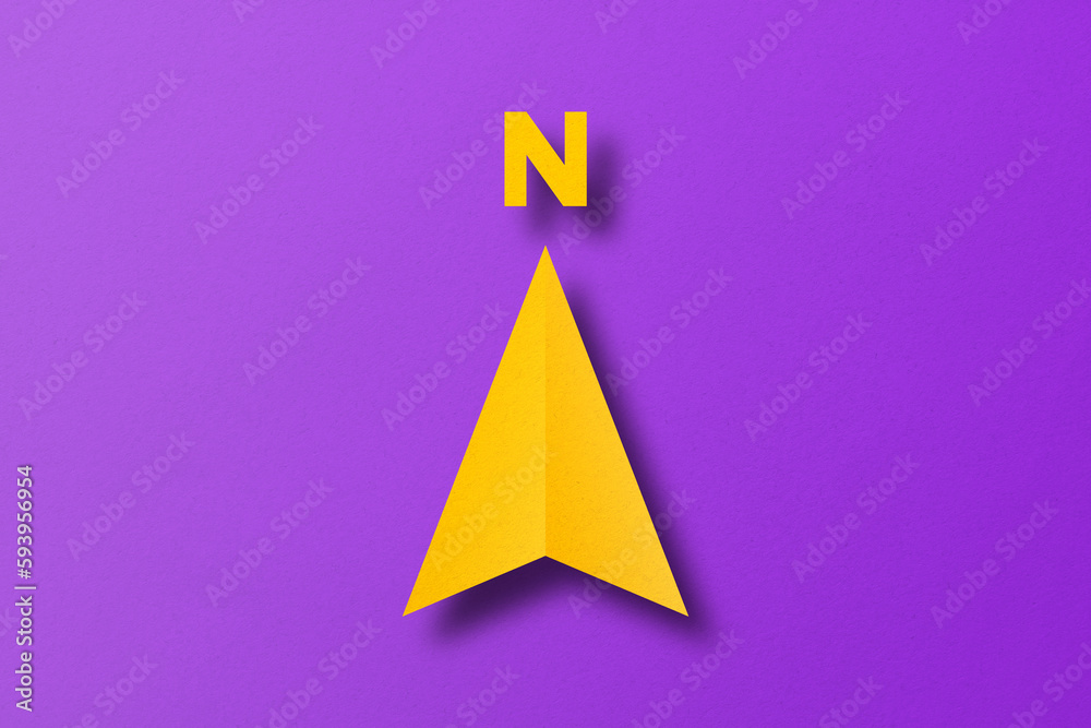 Yellow paper cut in north arrow shape set on purple paper background ...