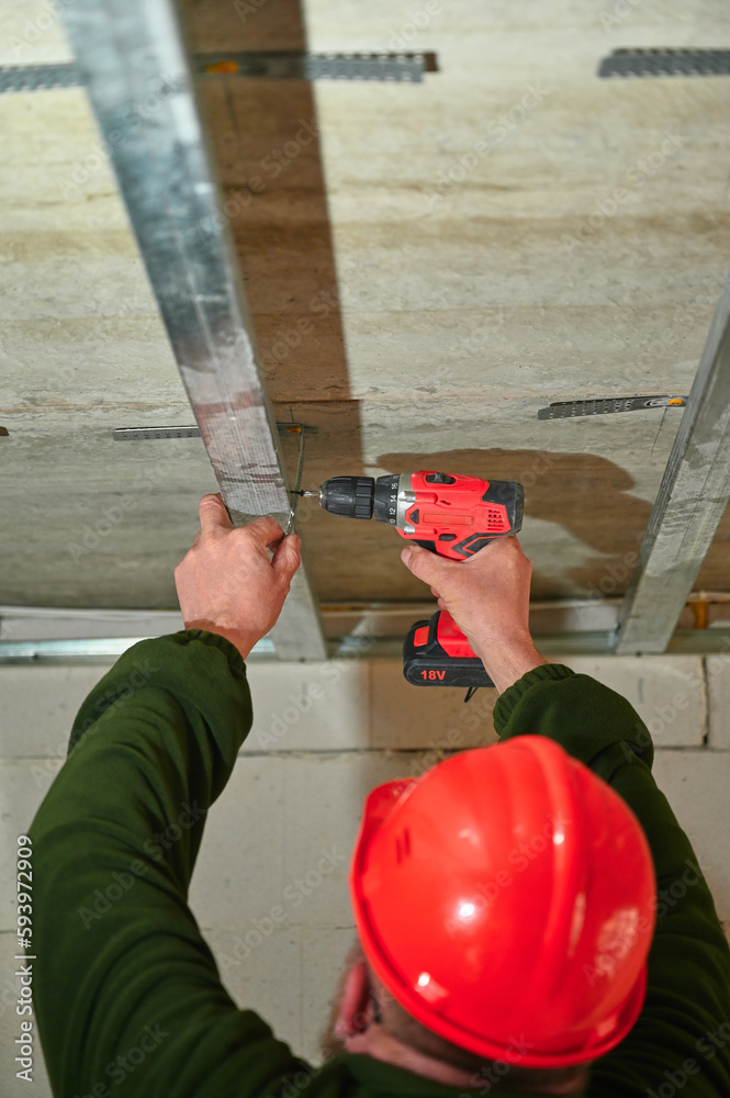A worker with an electric screwdriver installs a metal structure for ...
