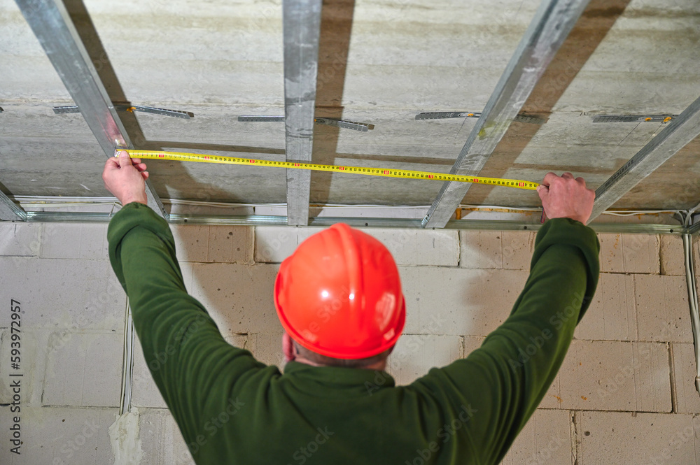 A worker with water level installs a metal structure for the ceiling ...