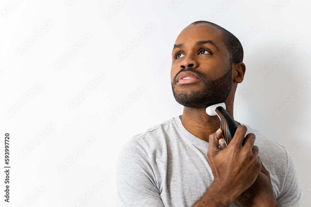 dark-skinned man is using an electric razor to shave his beard on a ...