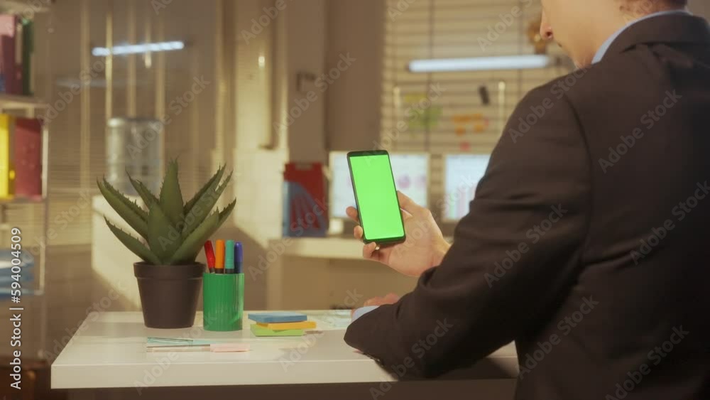 Back view of a young man is holding a mobile phone with a green screen ...