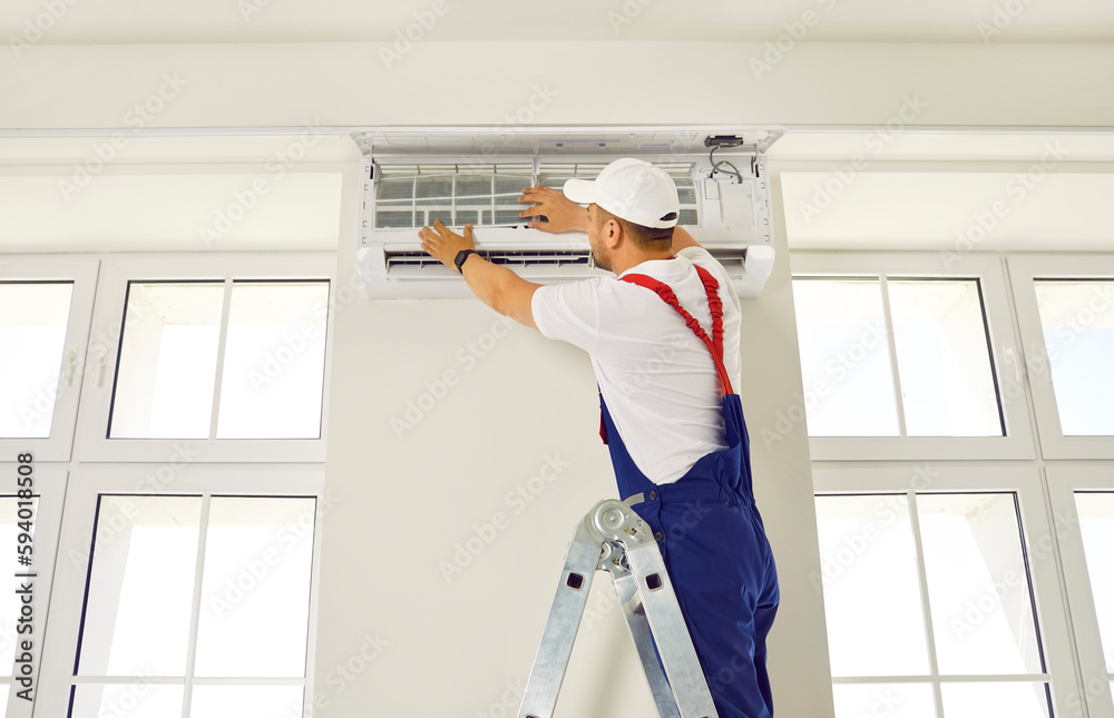 Foto de Worker installs ventilation system in office from ladder ...