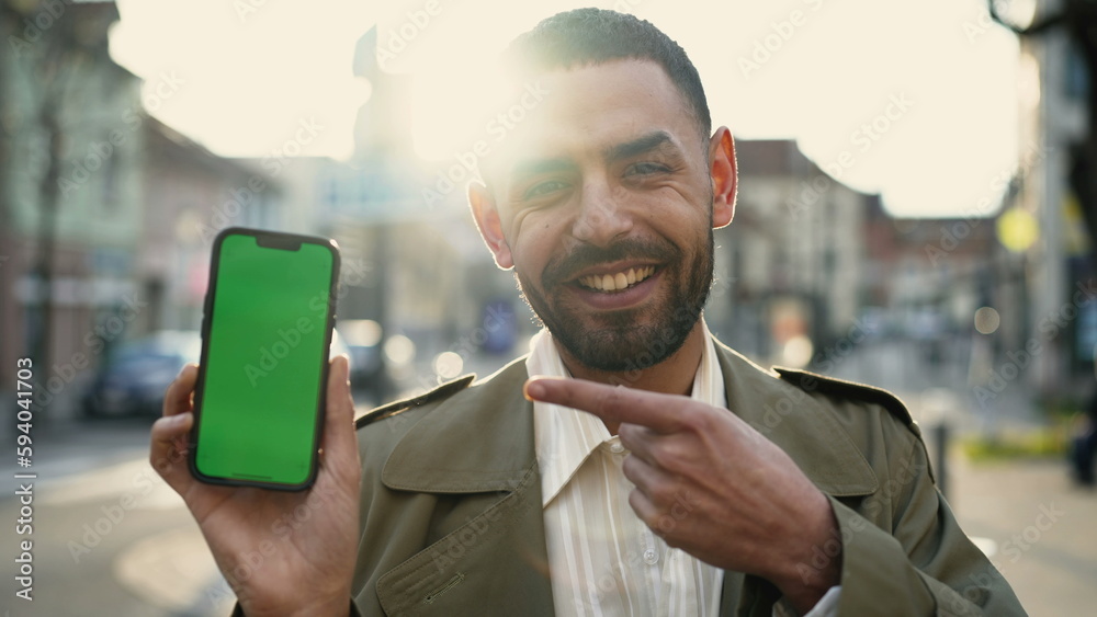 One cheerful Arab guy pointing at phone with greenscreen in chroma key ...