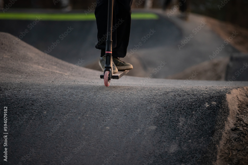 Closeup, the boy's legs with a stunt scooter in a skate park make jumps ...