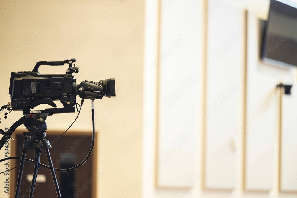 Professional video camera is set up on a tripod in a well-lit room ...