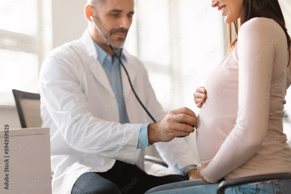 Male middle aged gynecologist with stethoscope examining belly of ...