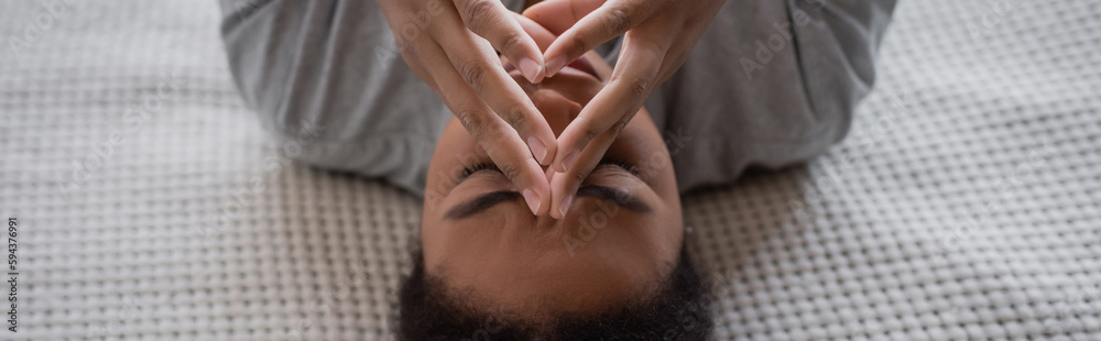 Sad multiracial woman touching face while lying on bed at home, banner ...