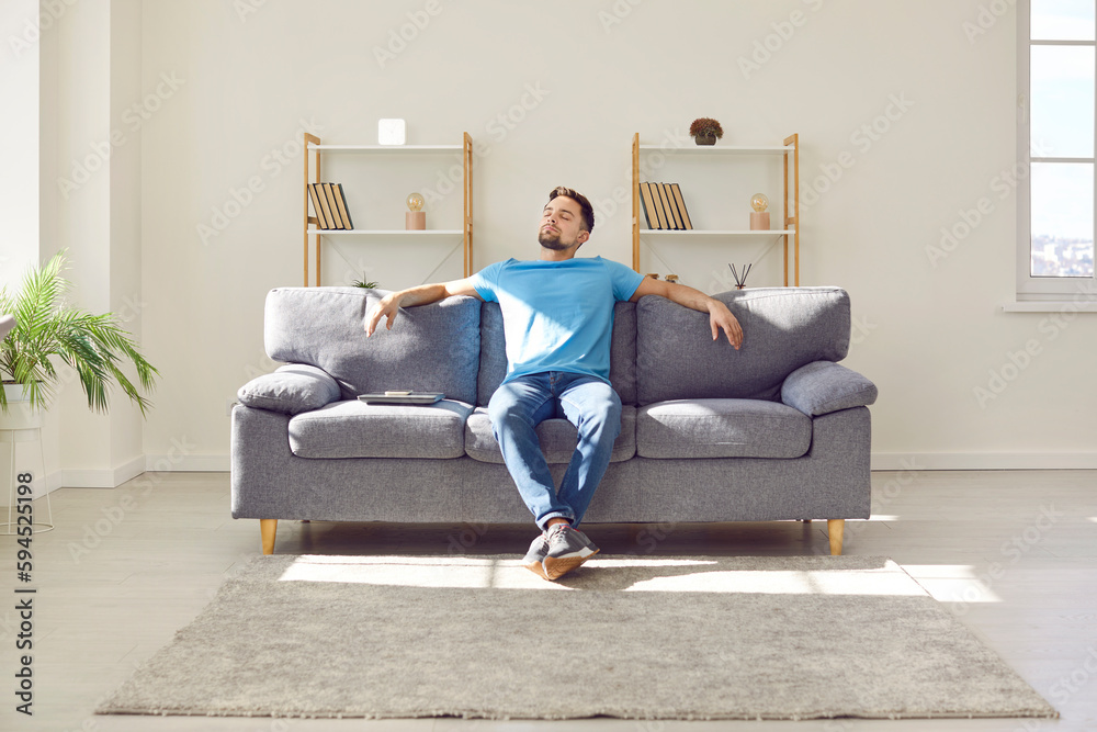 Young man relaxing on couch. Man enjoys his day off or takes pause while working. Relaxed man ...