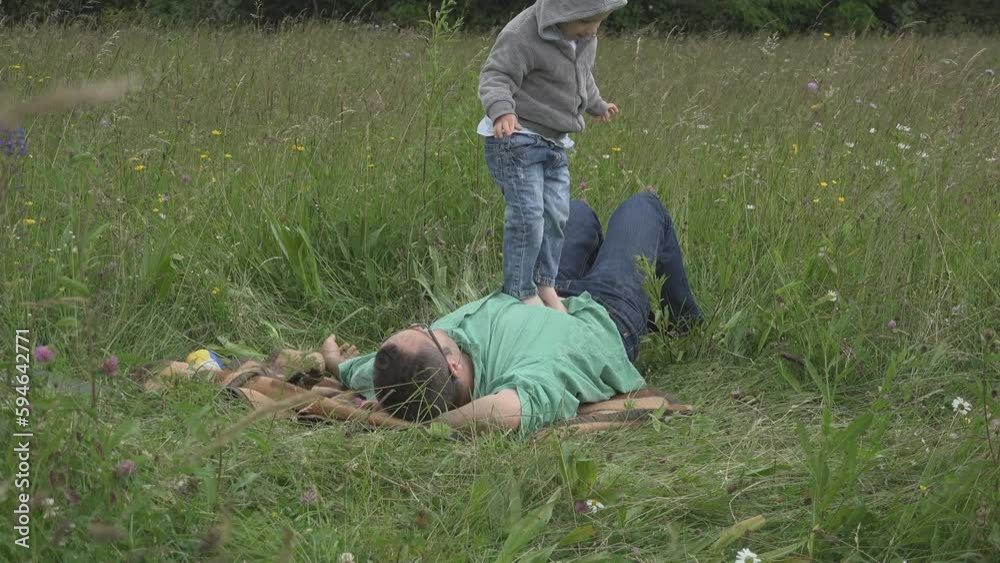 Little kid jumping from his father's belly lying down in the grass ...