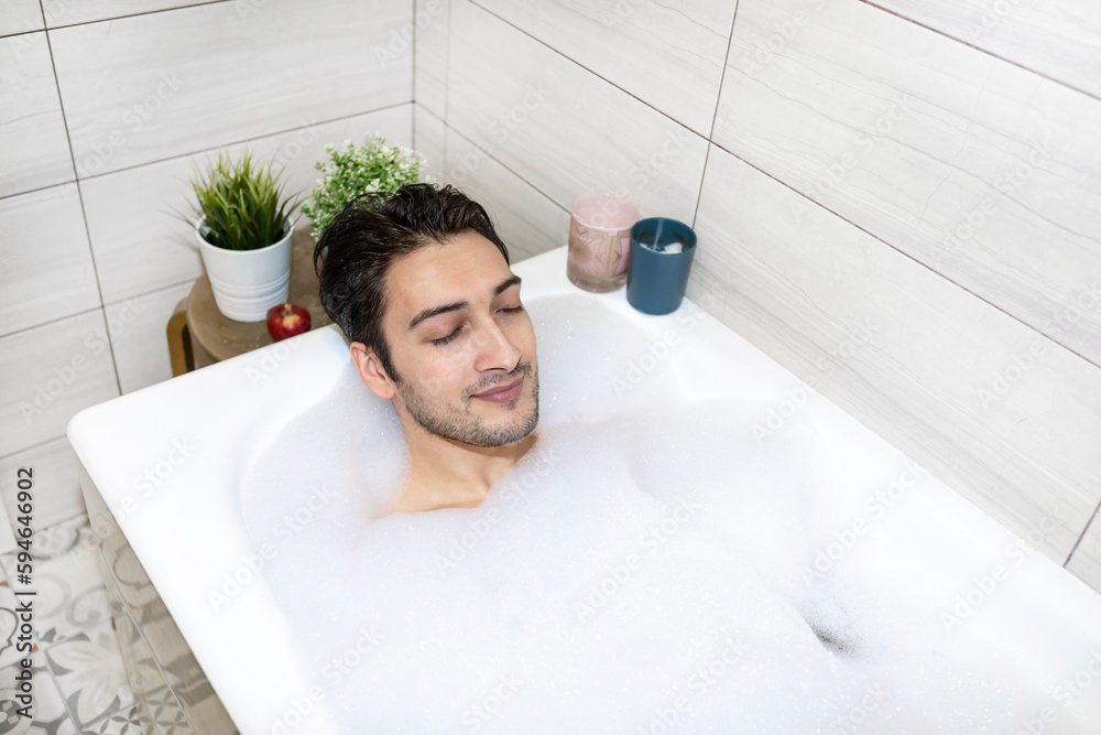 Handsome man lying and relaxing in the bathtub. Young guy bathing in ...