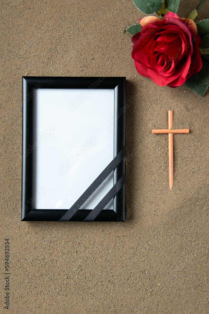 top view of stick cross with red flower and picture frame on the sand ...
