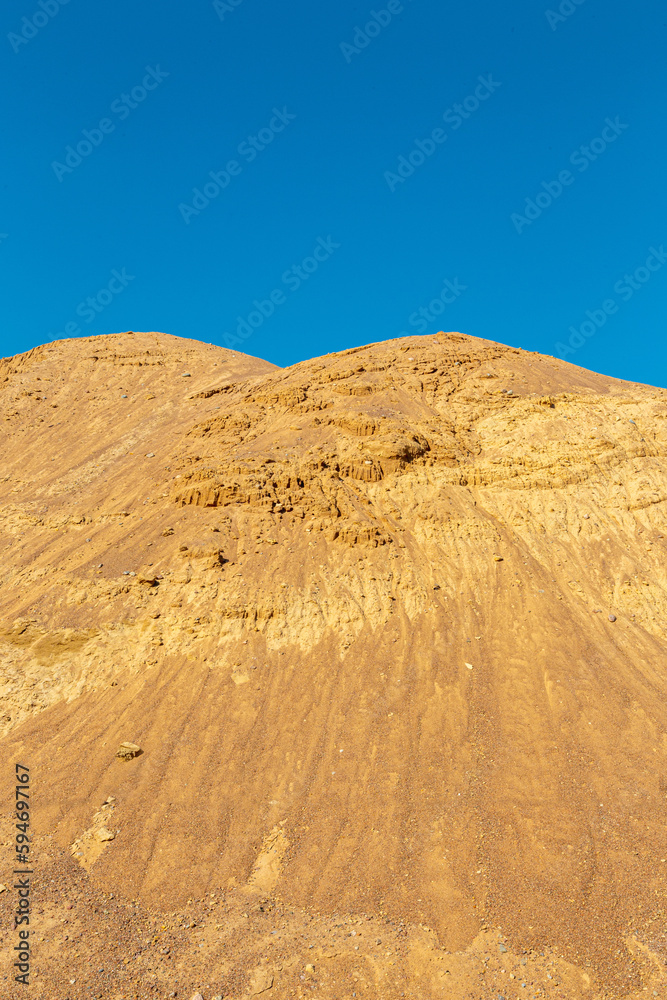 A high mountain of sand in a quarry against a blue sky. Stock of bulk ...