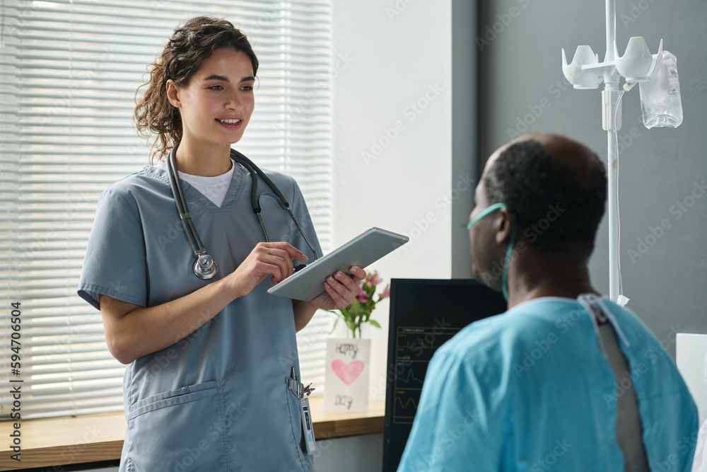 Young nurse using digital tablet while asking patient about his health ...