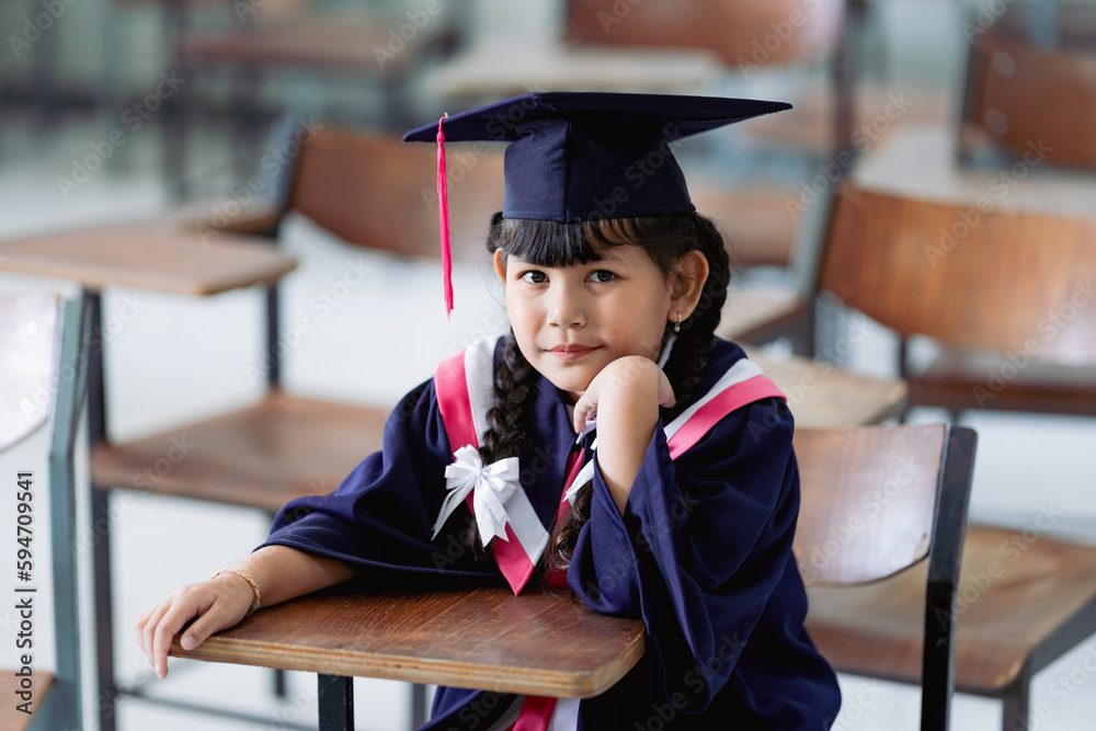 A cheerful kid graduate wearing an academic gown and graduation cap ...