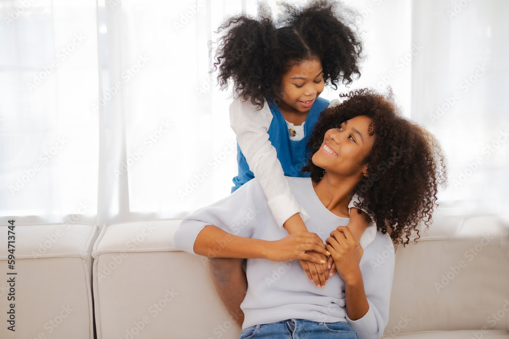 African American kid sitting over sofa embrass her mother neck, look in ...